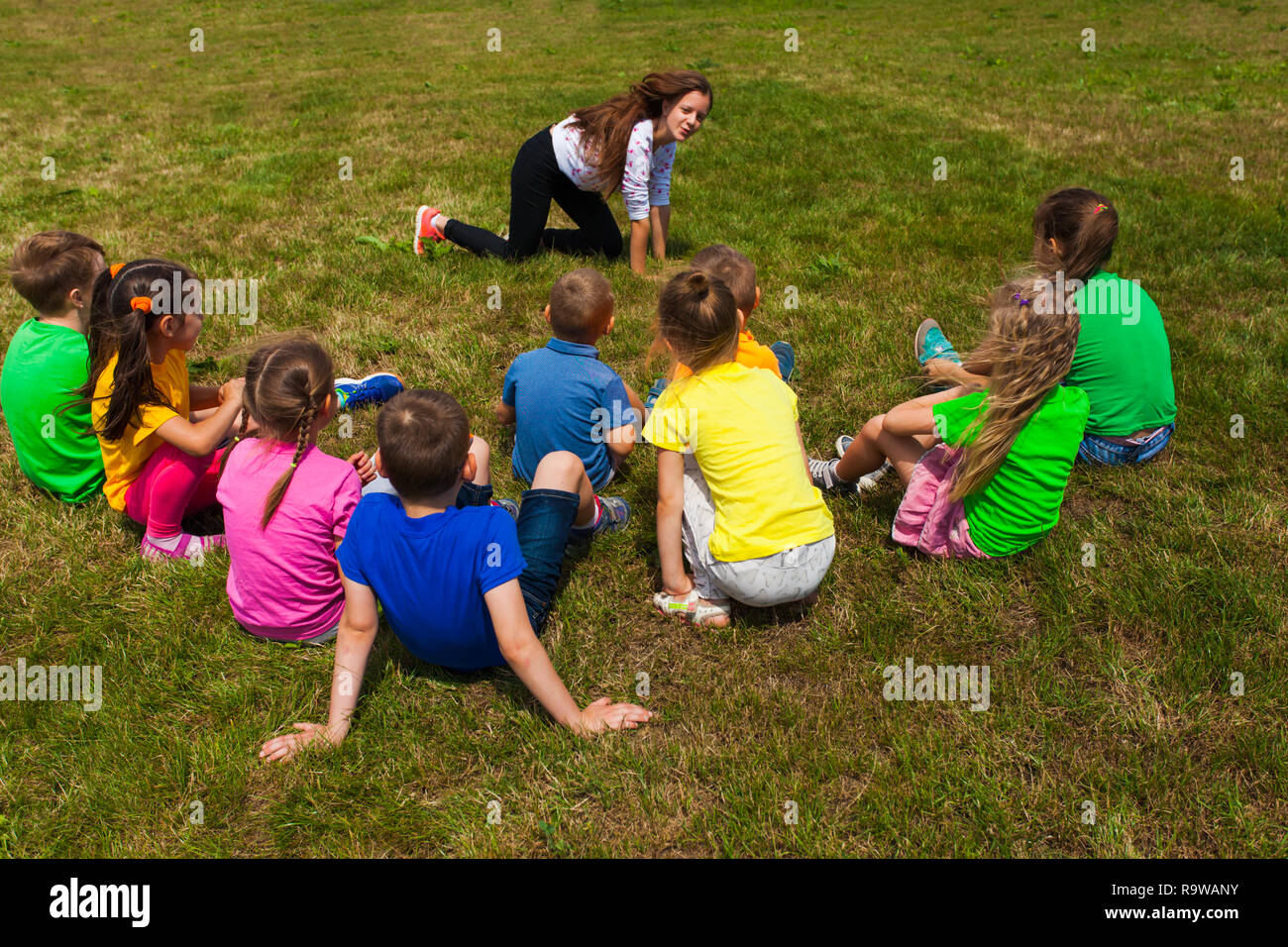 Back view of kids sitting on a grass playing charades Stock Photo - Alamy