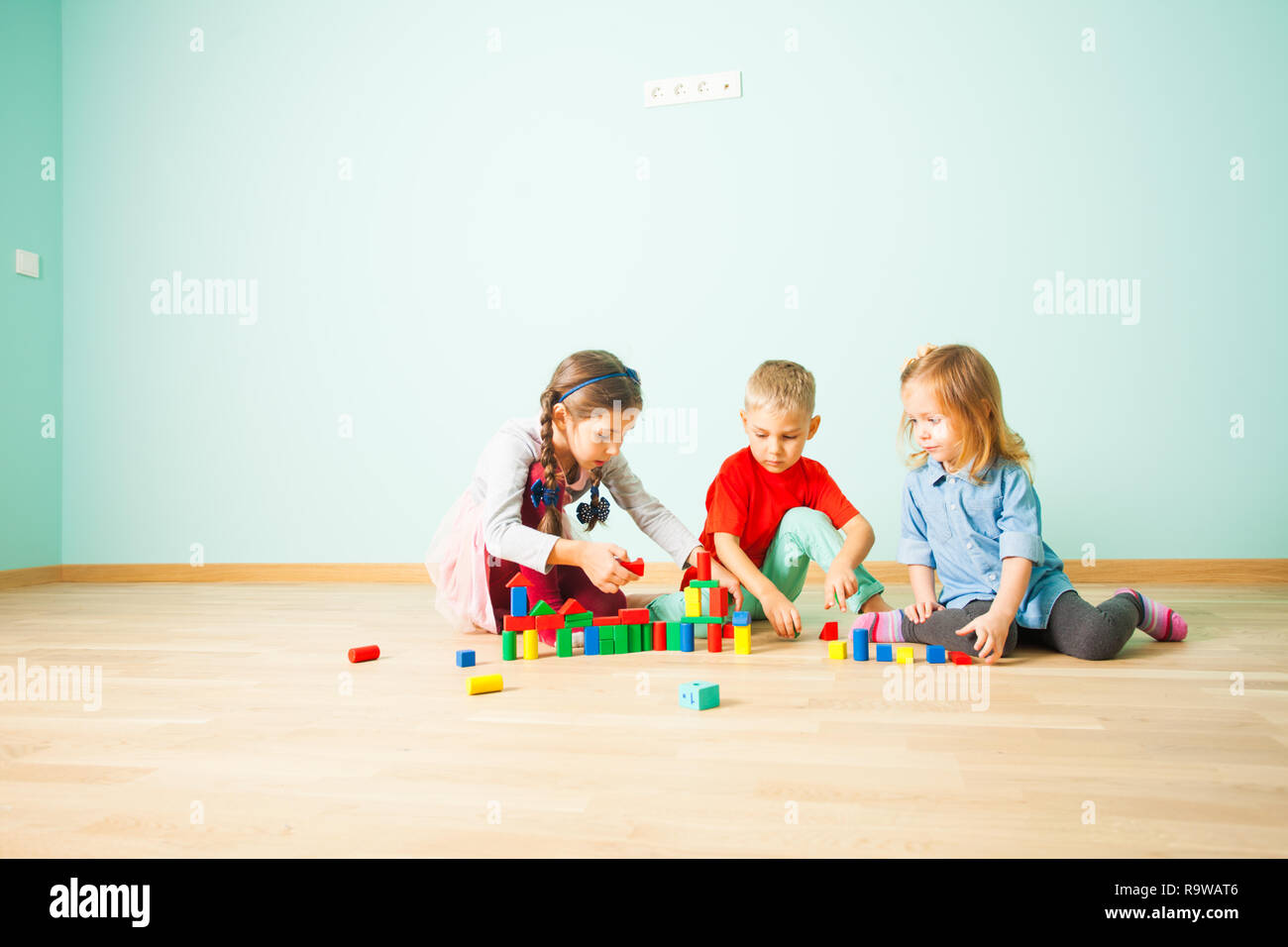 Three friends building with blocks on a floor Stock Photo - Alamy