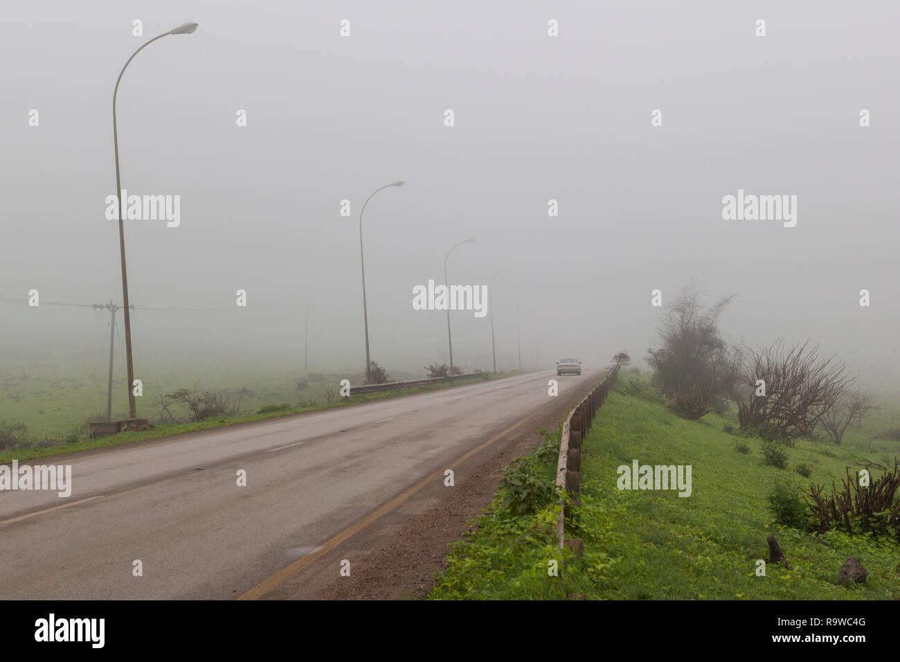 A road cuts through the misty green landscape near Salalah, Dhofar ...