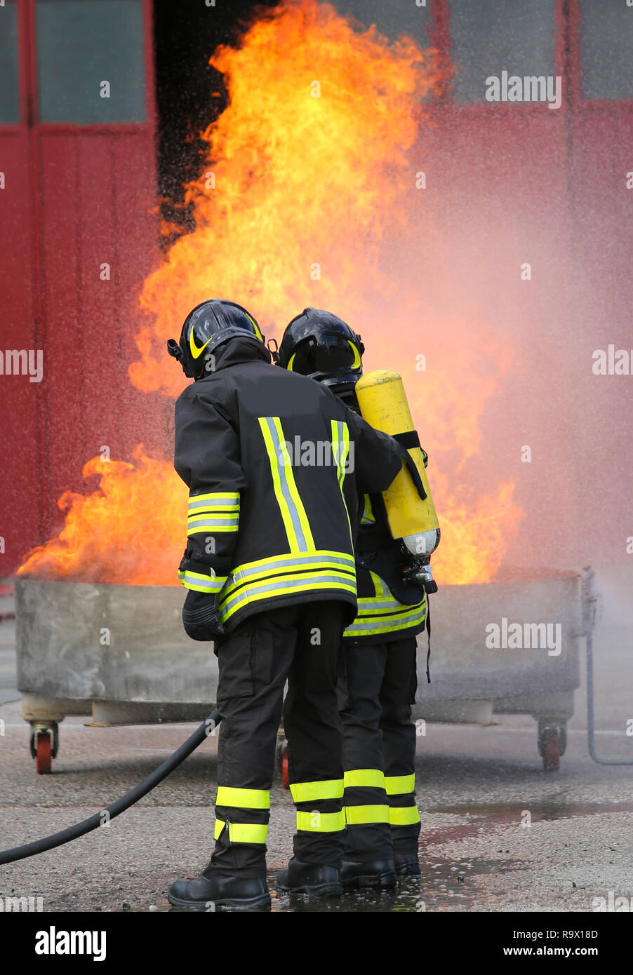 two brave firefighters during the exercise with a tank full of flames ...