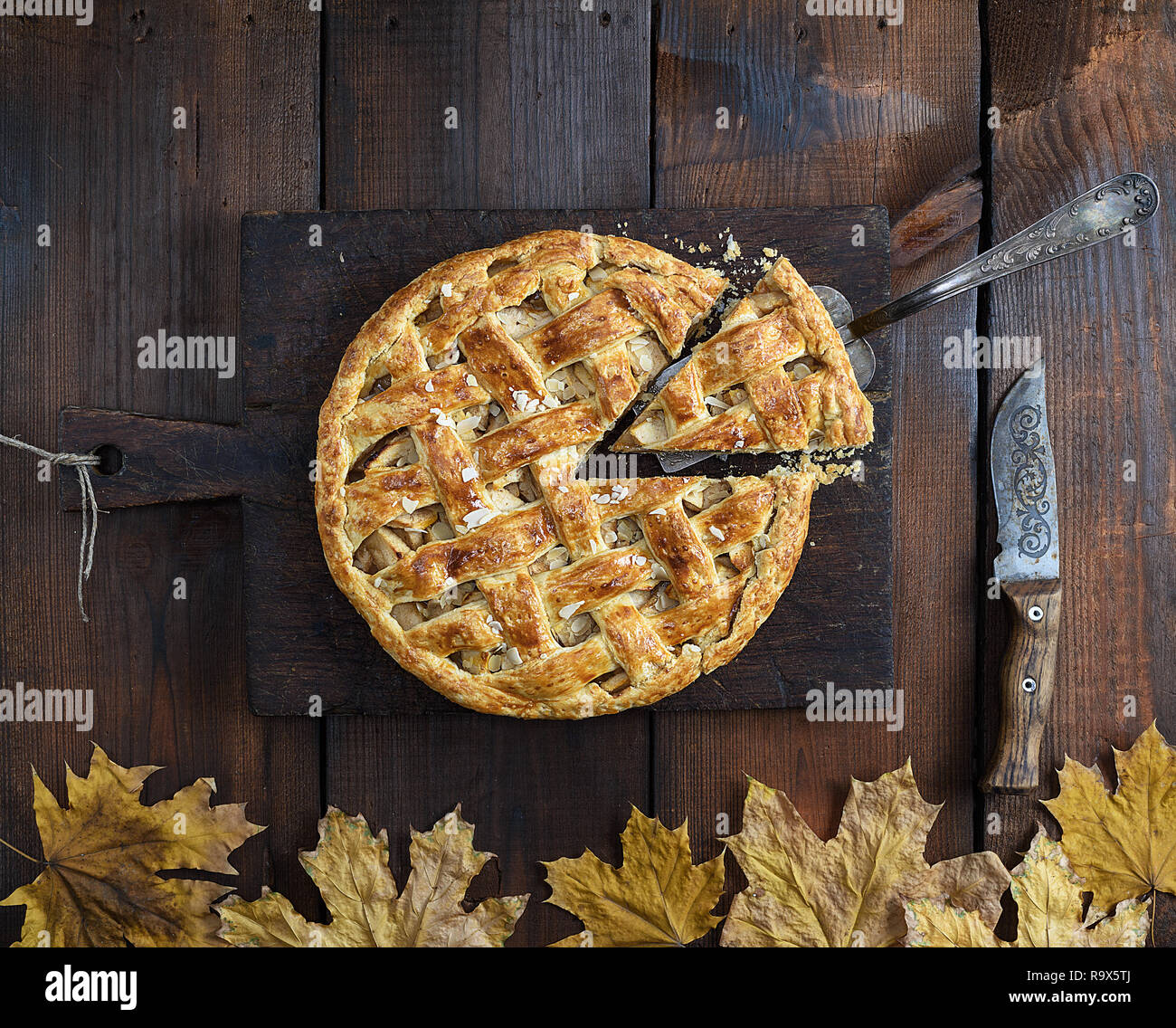 baked whole round apple pie on a rectangular old brown cutting board ...