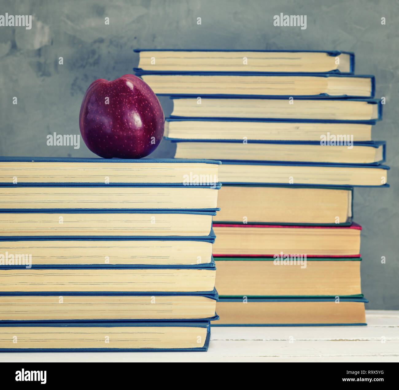 ripe red apple on a stack of books with a blue cover Stock Photo - Alamy