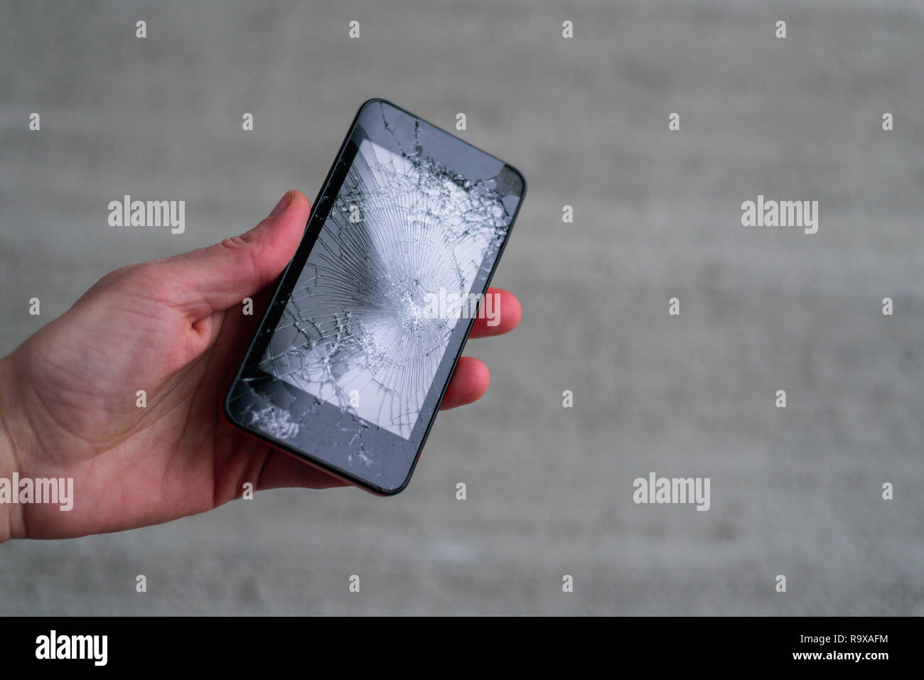 Hand holding phone with broken screen by hammer Stock Photo - Alamy