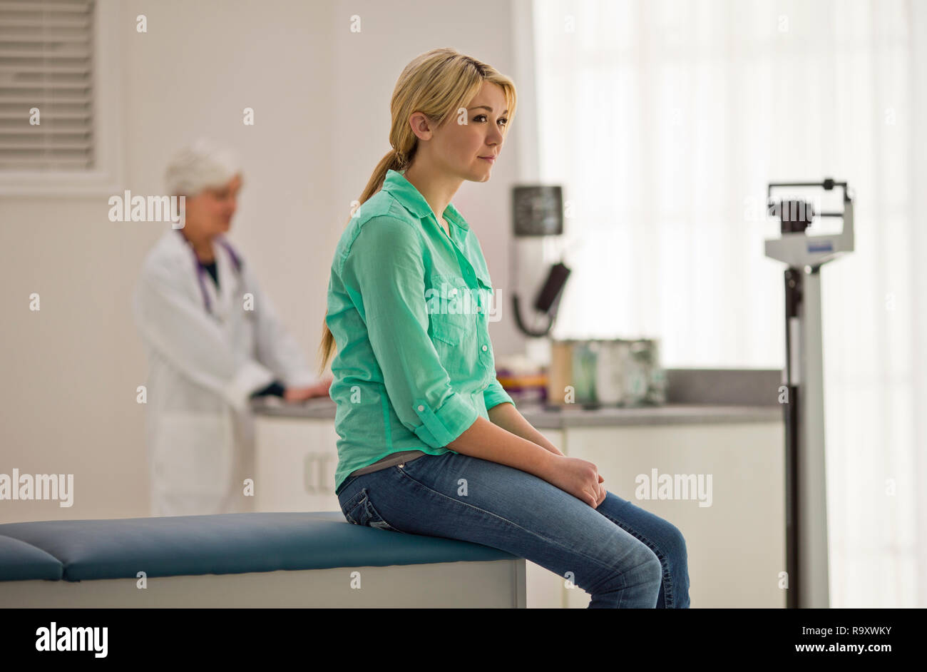 Contemplative young woman sitting inside a doctor's office with a ...
