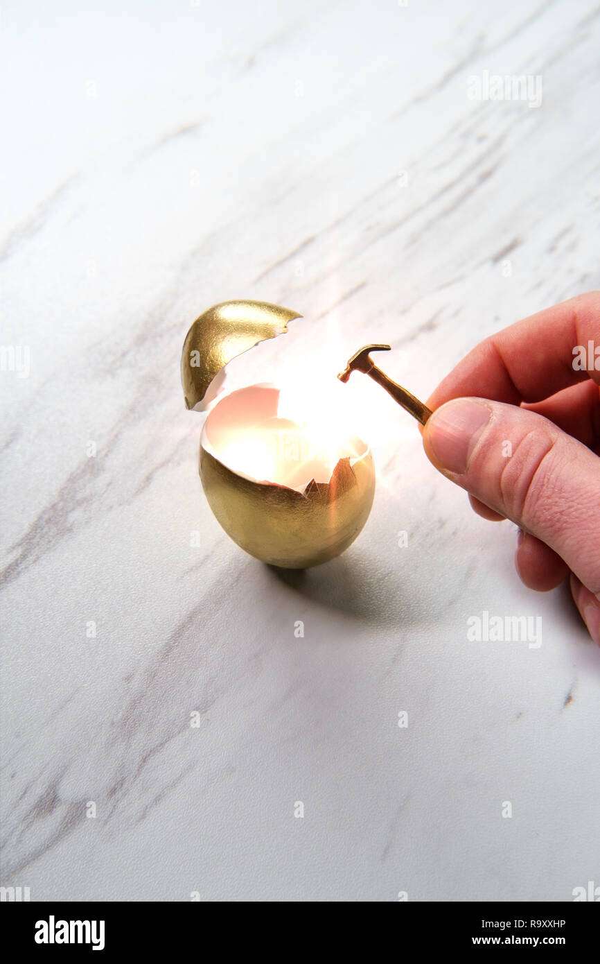 Tiny hammer breaks golden egg with shattered shell pieces action Stock ...