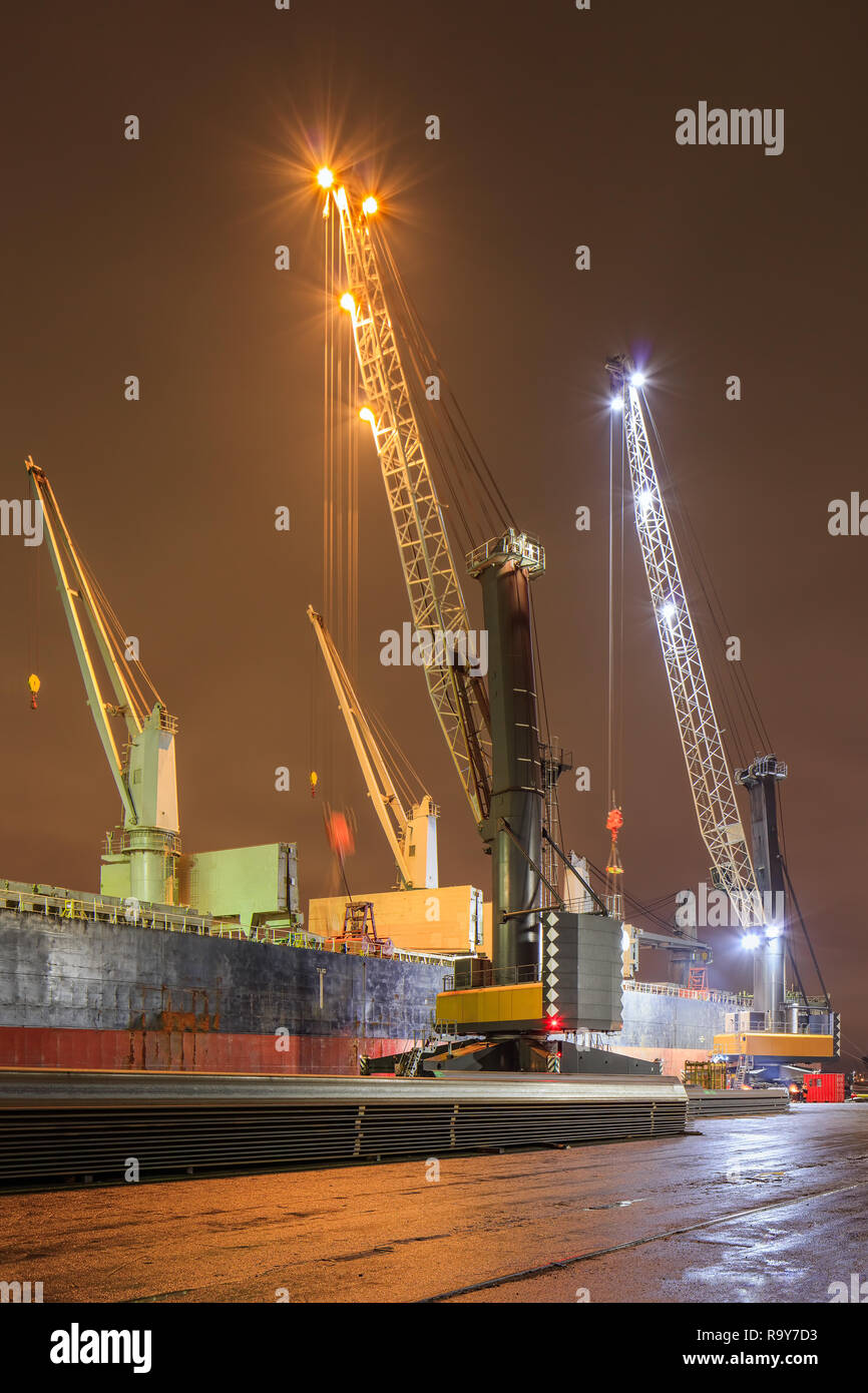Night scene with cranes on illuminated quay loading a moored vessel ...