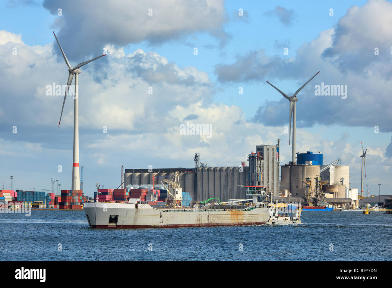 Hopper barge assisted by a tug boat with industrial area on the ...