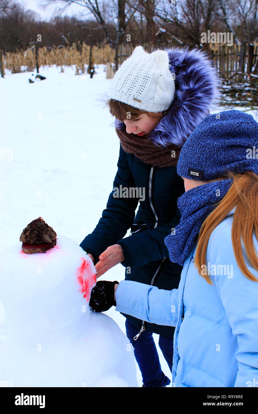 Two girls make snowman in winter. Children make snowman. Two sisters ...