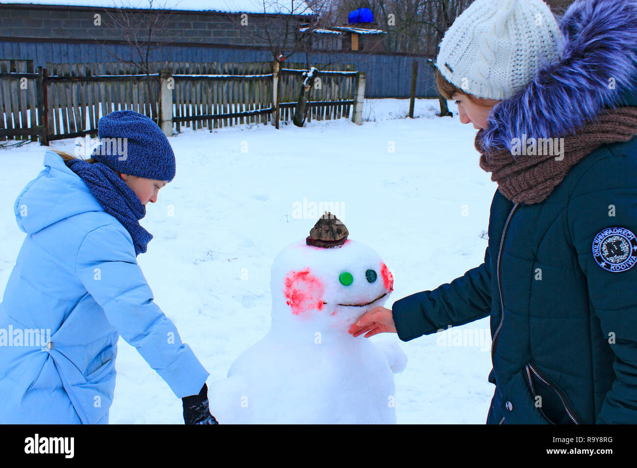 Two girls make snowman in winter. Children make snowman. Two sisters ...