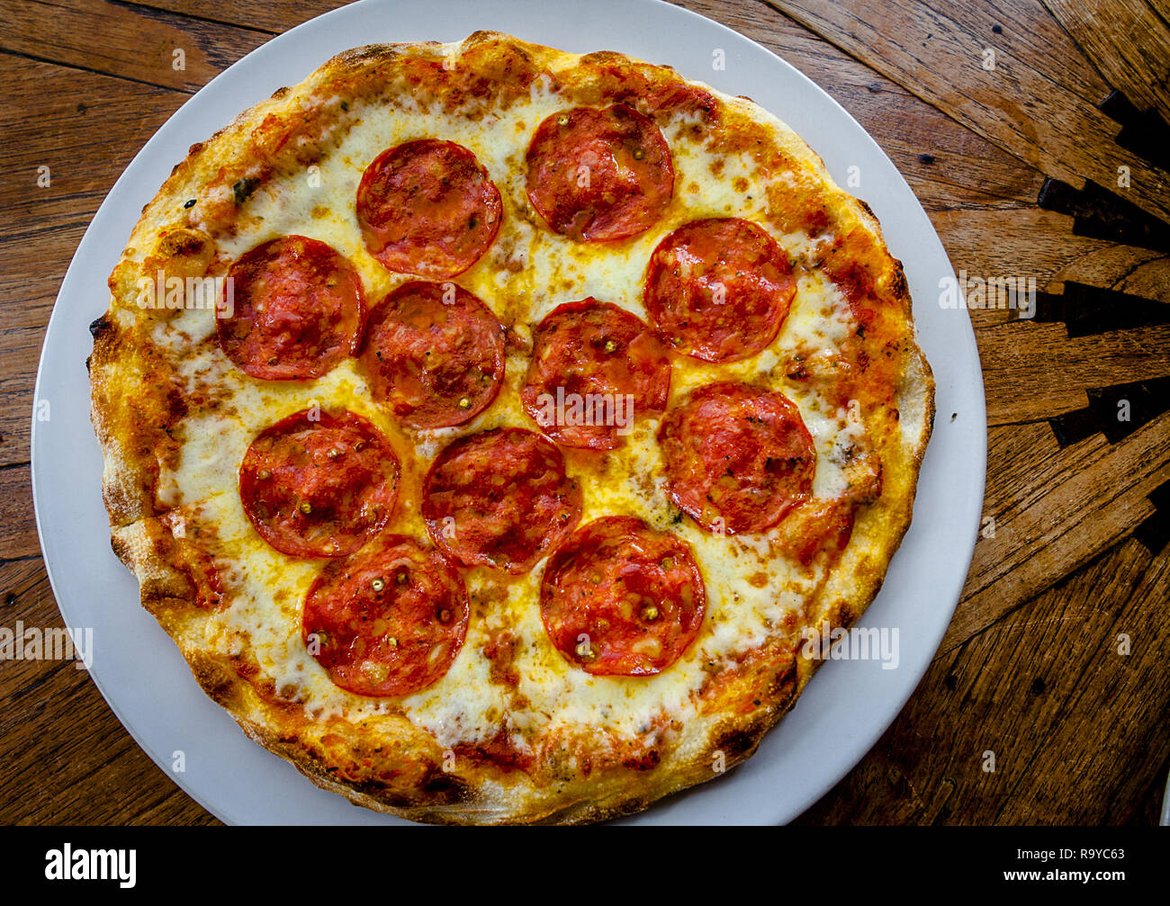 Round whole pepperoni pizza served on a plate sitting on a wood grained ...