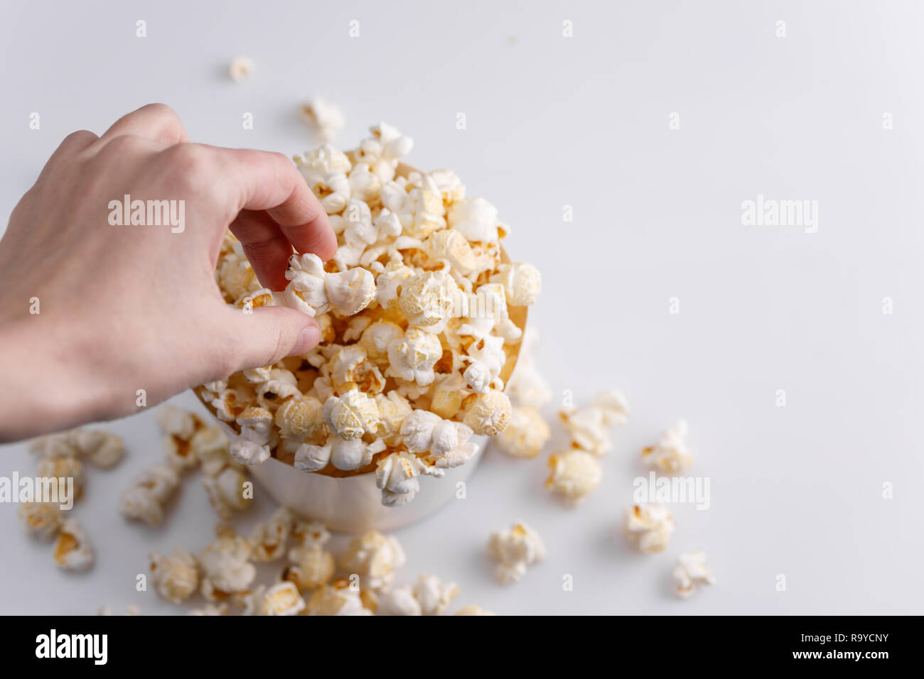 A hand is taking a popcorn from a paper bucket on a white background ...