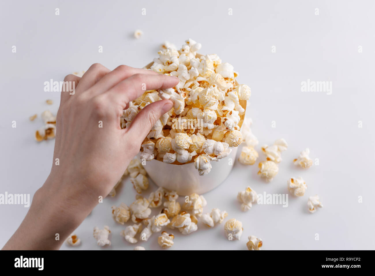 A hand is taking popcorn from a full paper bucket on a white background ...