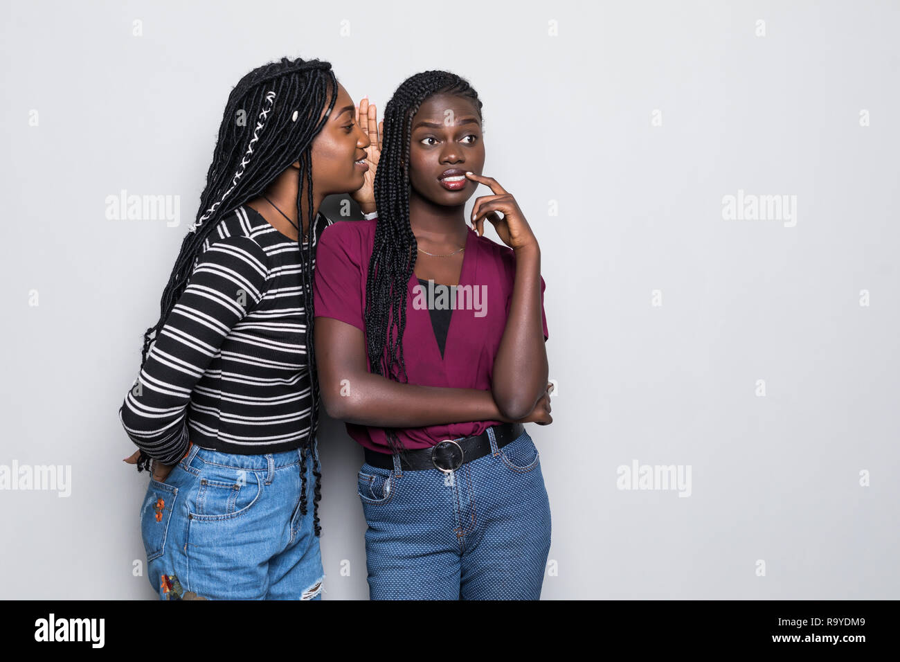 Portrait of two happy young african women sharing secrets over white ...