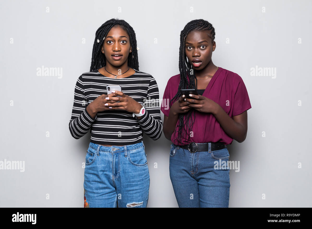 Portrait of two cute african women using cell phones with surprise over ...