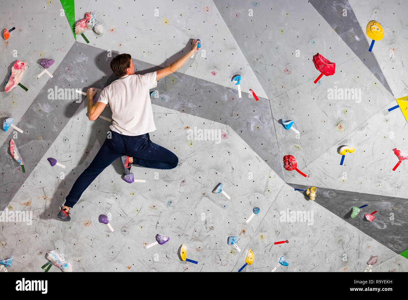 Rock climber man hanging on a bouldering climbing wall, inside on ...