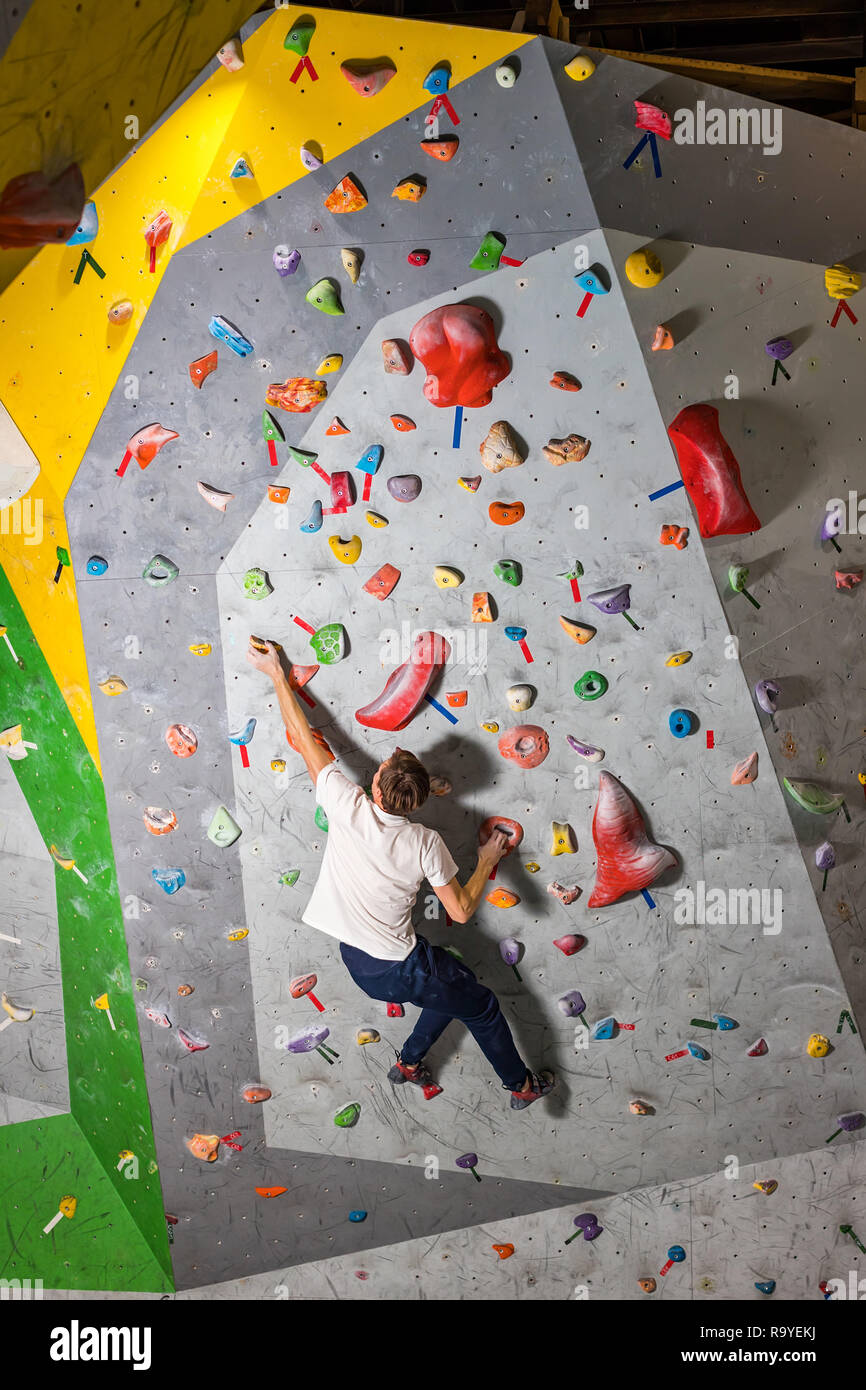 Rock climber man hanging on a bouldering climbing wall, inside on ...