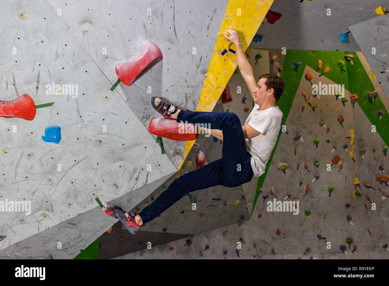 Rock climber man hanging on a bouldering climbing wall, inside on ...
