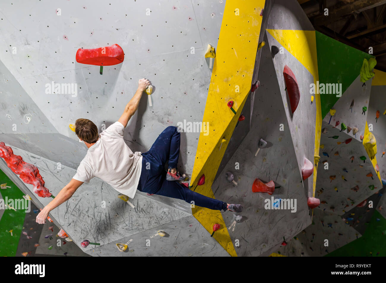 Rock climber man hanging on a bouldering climbing wall, inside on ...