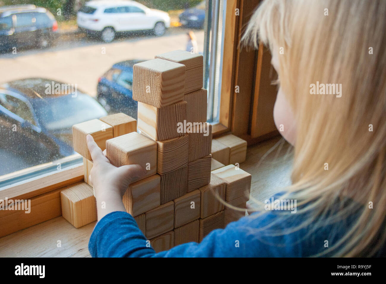 Child playing with wooden blocks or cubes at home by the window ...