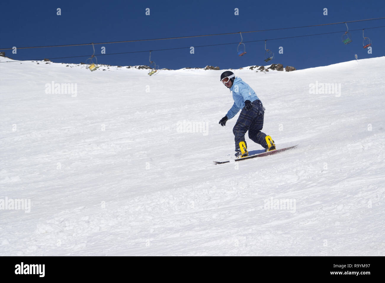 Snowboarder riding on snowy ski slope at high winter mountains in sunny day. Caucasus Mountains ...