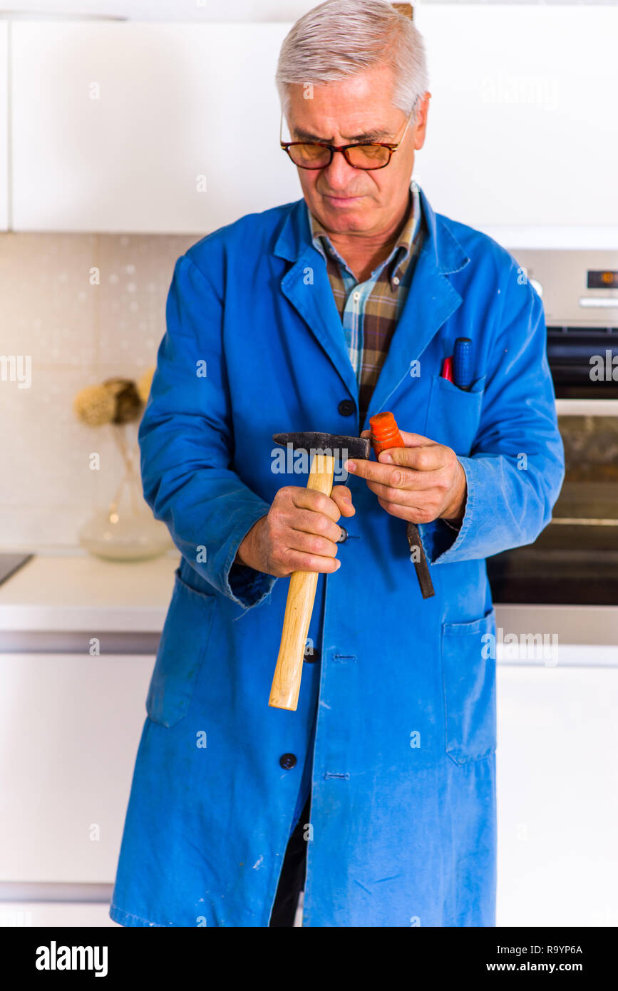 An old age handyman in overall is standing in the kitchen with his ...