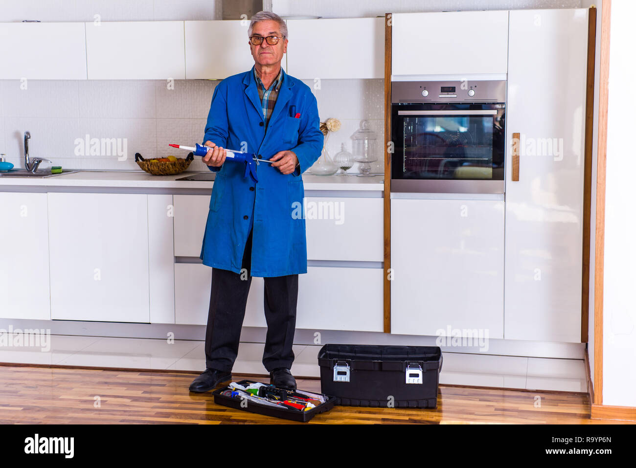 An old age handyman is standing in the kitchen with his tools on the ...