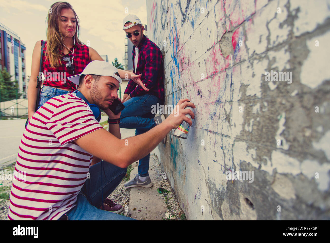 Three young friends having fun while drawing graffiti on the wall with ...