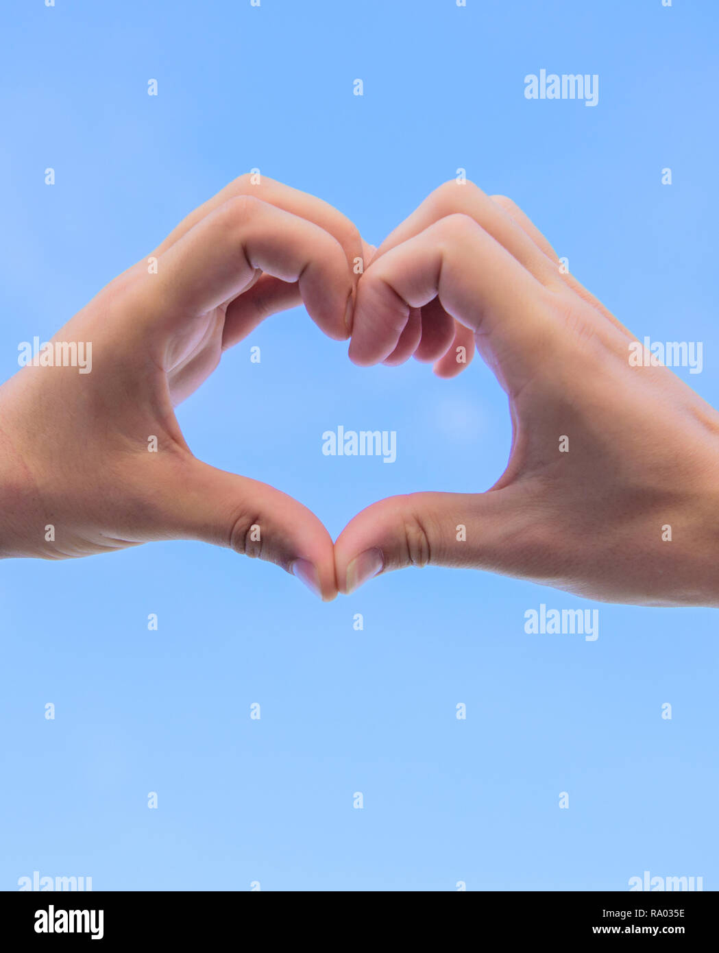 Hands put together in heart shape blue sky background. Love symbol ...