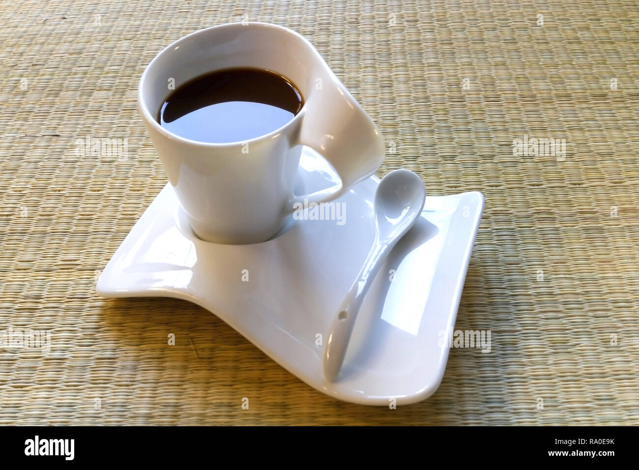 French designed coffee cup with black coffee, small stirr spoon on tan ...
