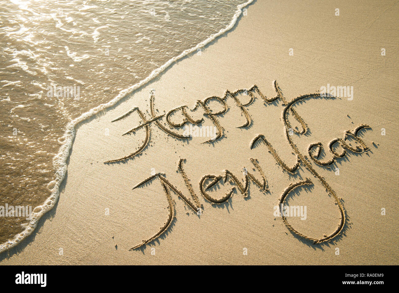 Happy New Year message handwritten on smooth sand beach with incoming ...