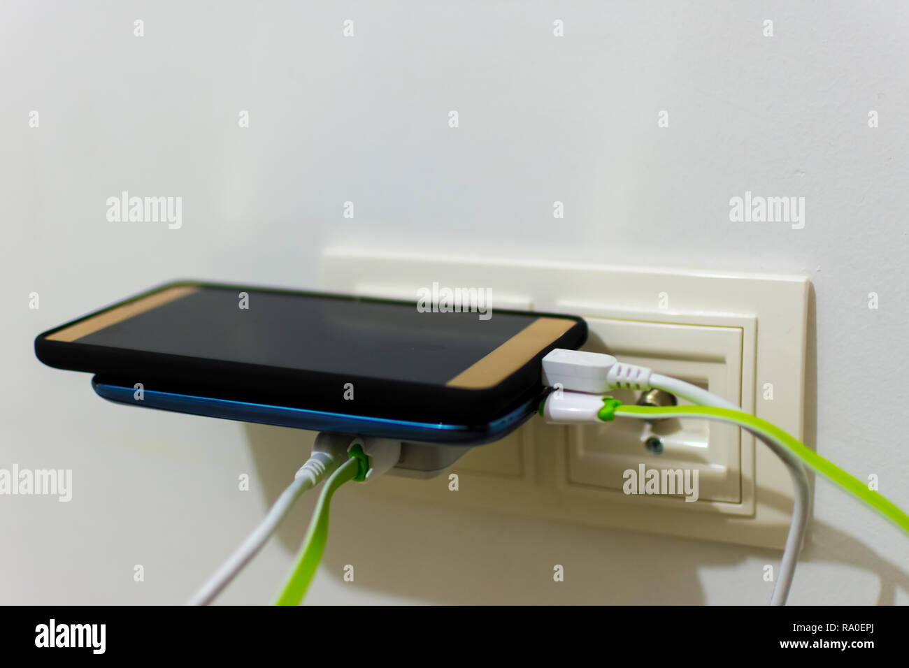 Two mobile phones charging plugged into the charger Stock Photo - Alamy