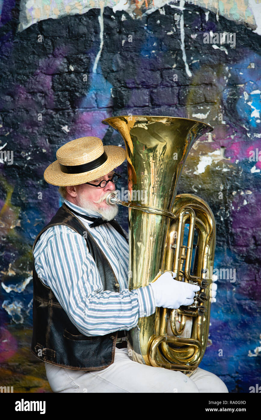 Man playing a tuba in front of graffitied wall Stock Photo - Alamy