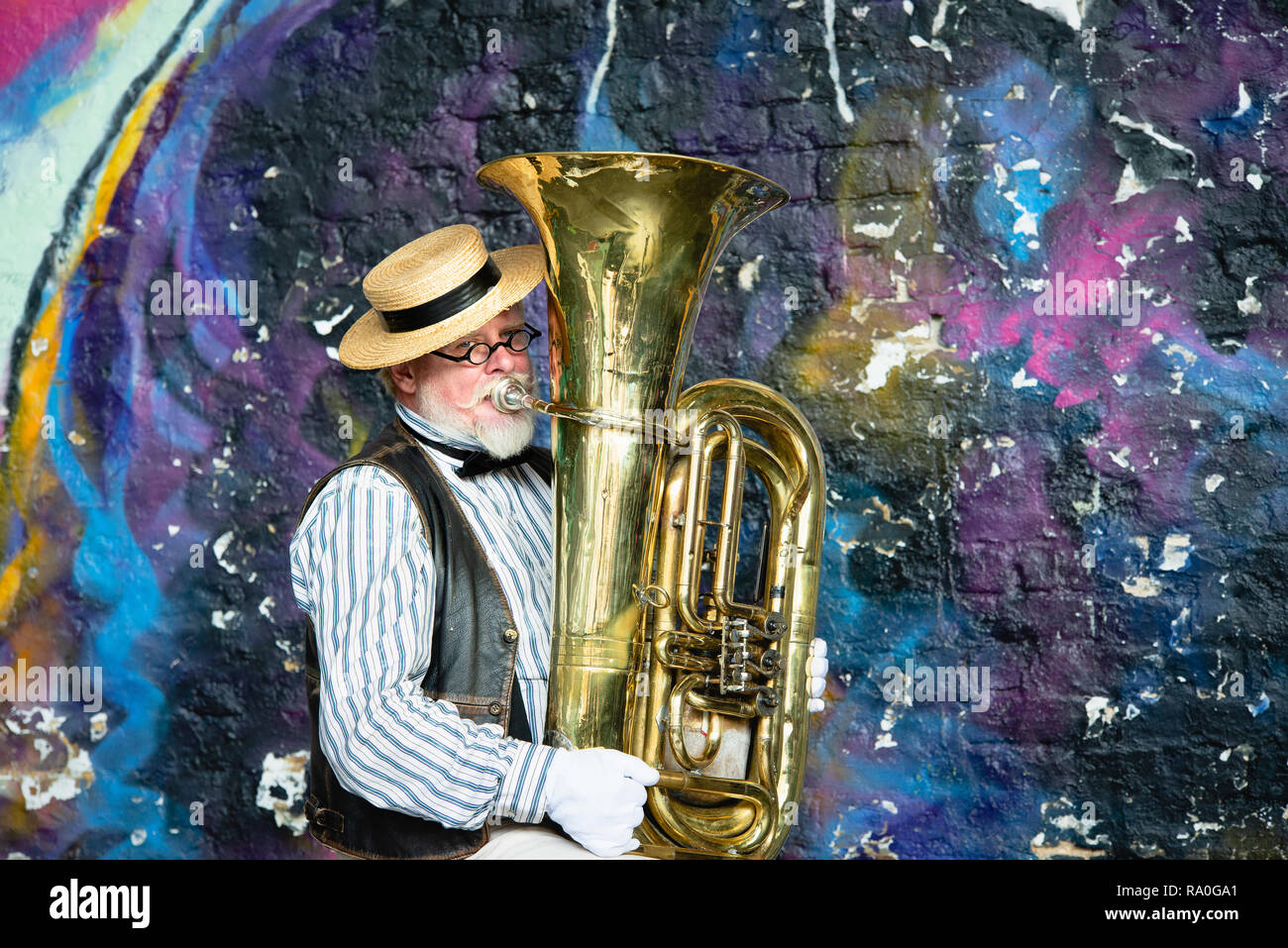Man playing a tuba in front of graffitied wall Stock Photo - Alamy