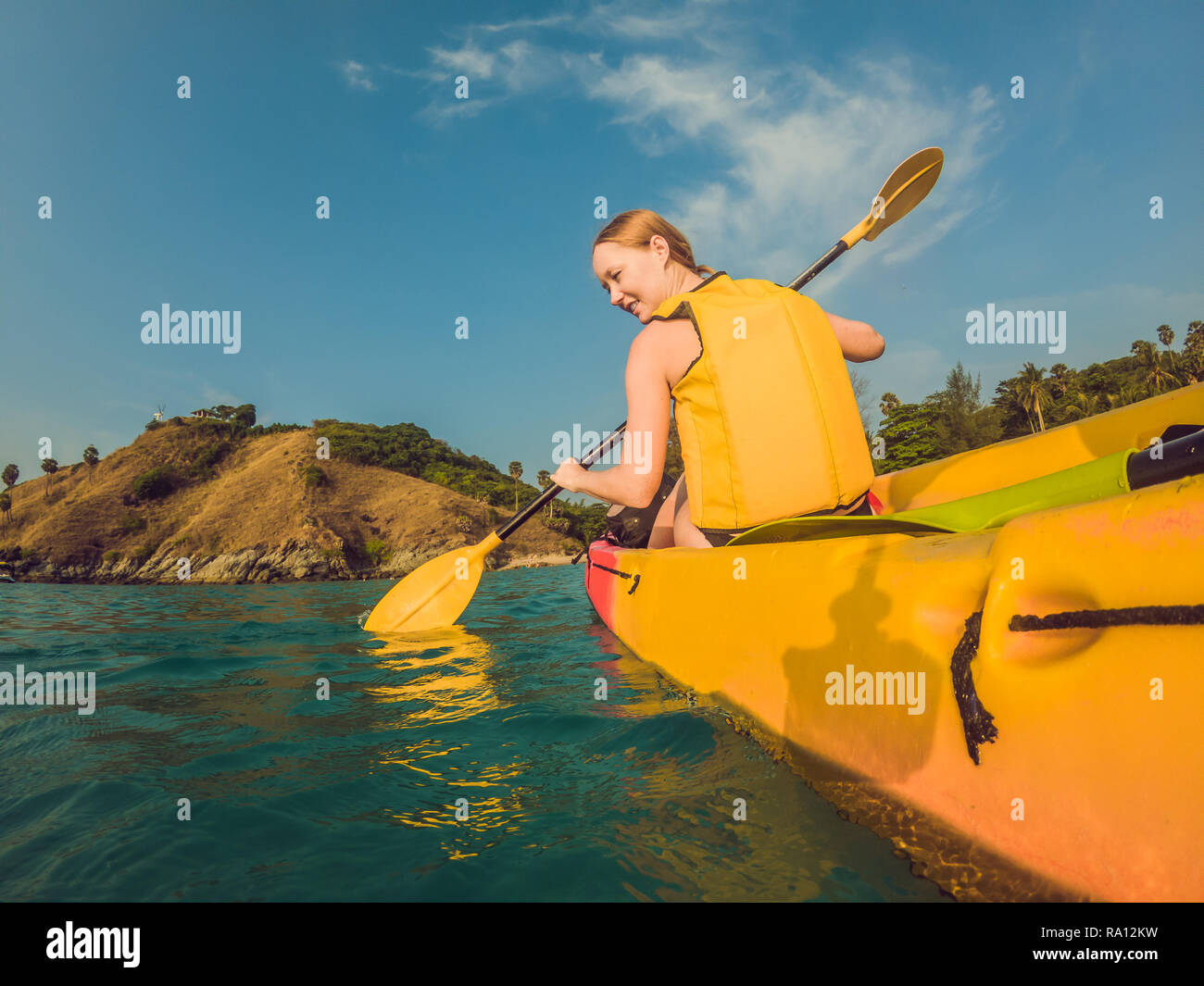 Smiling young woman kayaking on sea. Happy young woman canoeing in sea ...