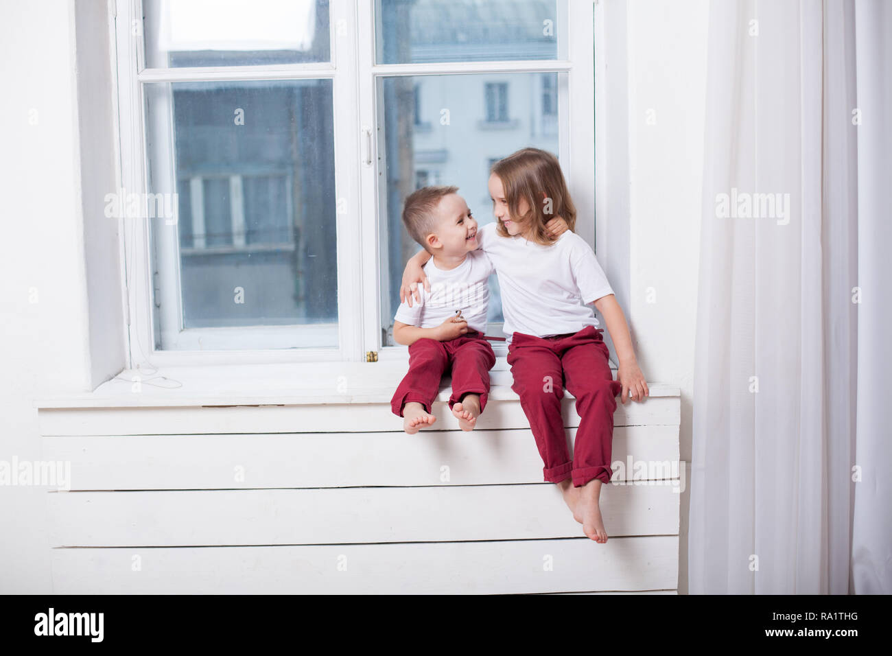 boy and girl are brother and sister sit on the windowsill at the window ...