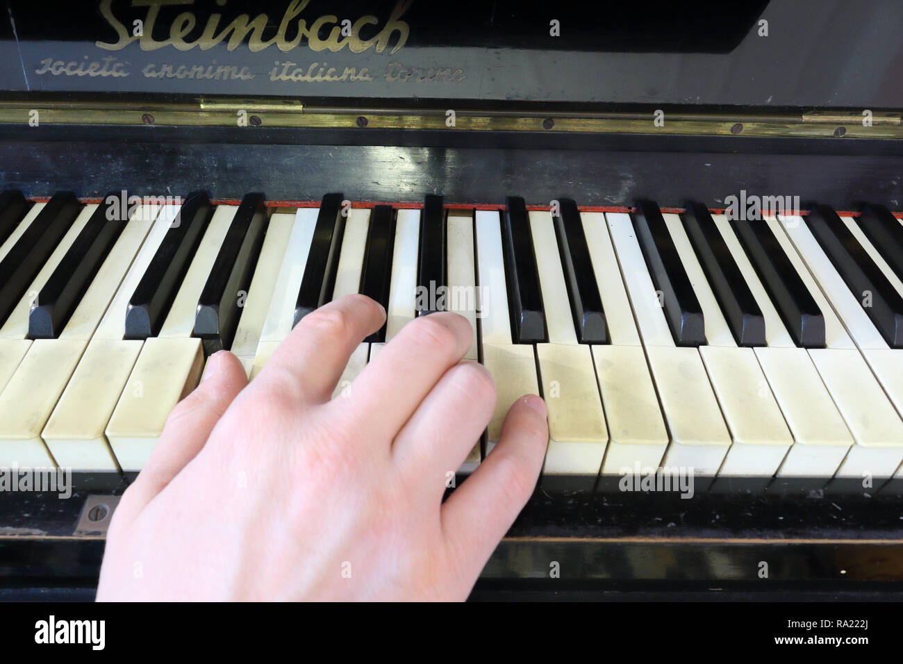 A right hand playing a E (MI) major chord on an old black piano with ...