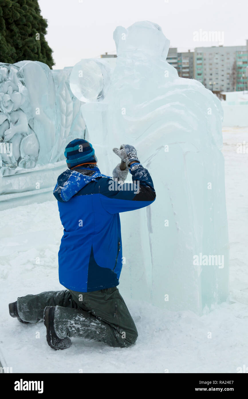 The sculptor cuts an ice figure for Christmas from a block of ice with ...