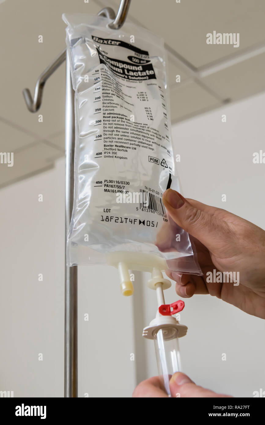 Nurse attaches a giving set to a bag of saline to administer to a ...