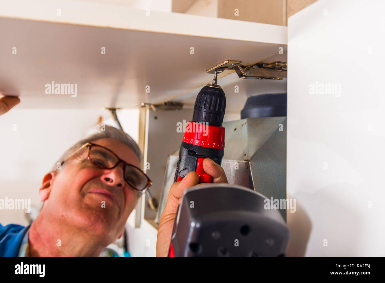 Old age handyman is standing in the kitchen and working with power ...