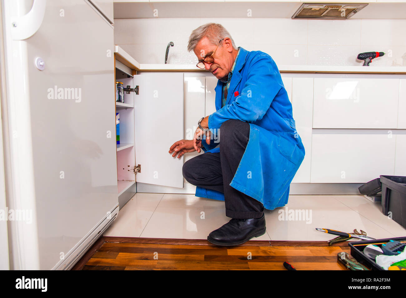 Serious handyman is standing in the kitchen and fixing the cupboard ...