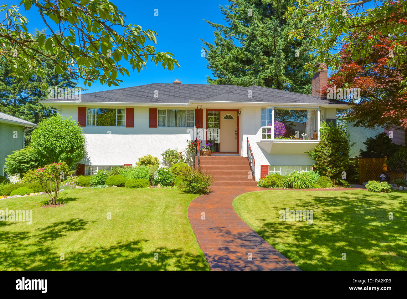 Average family house with green lawn and trees in front on blue sky ...