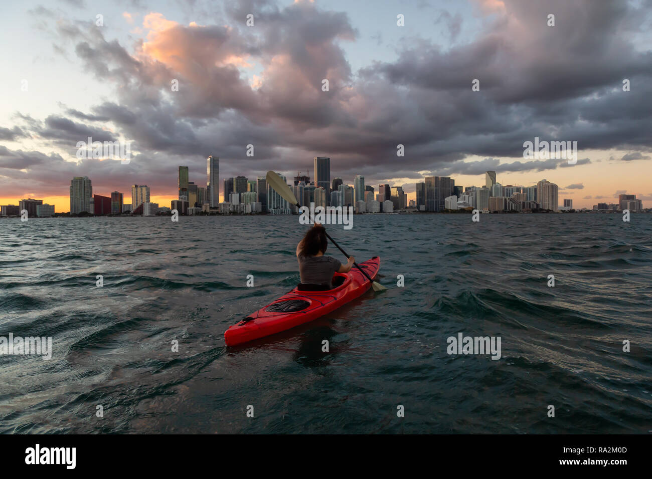 Adventurous girl kayaking in front of a modern Downtown Cityscape ...
