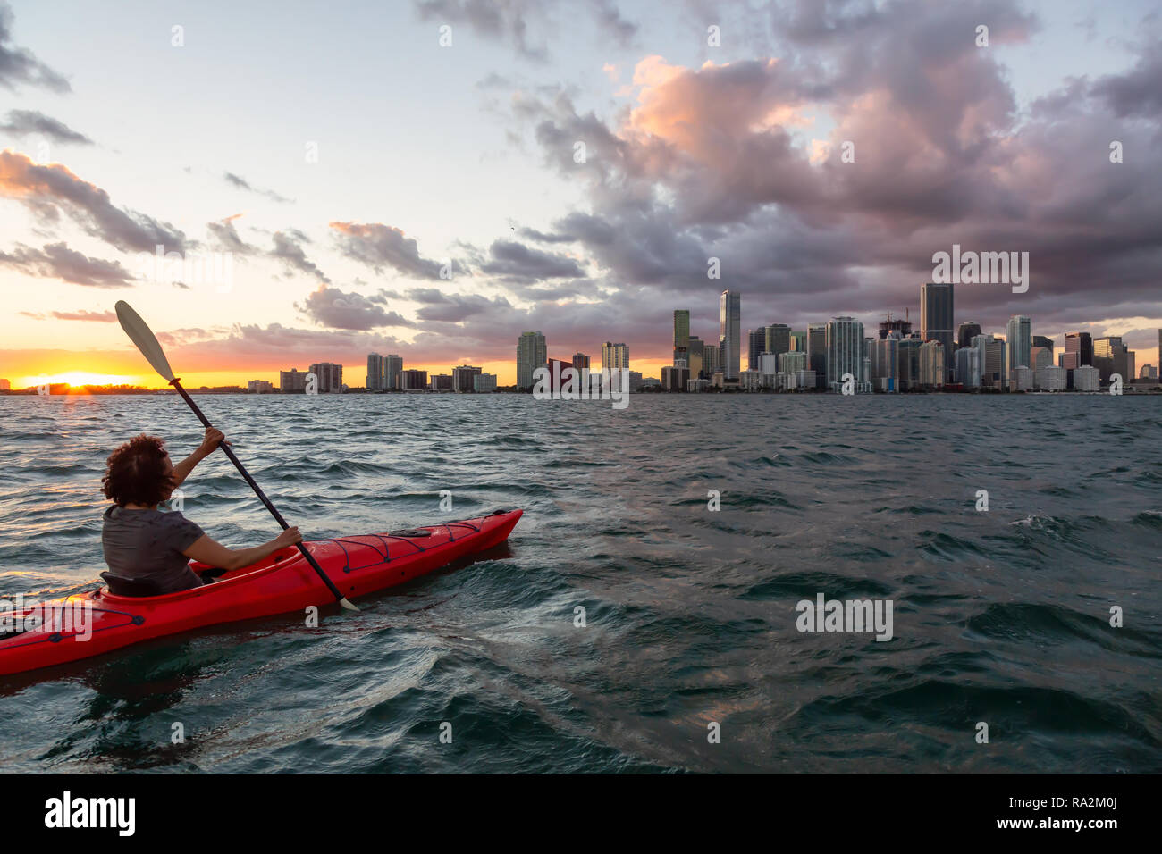 Adventurous girl kayaking in front of a modern Downtown Cityscape ...