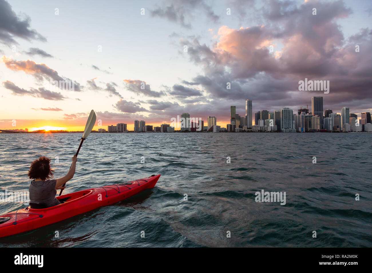 Adventurous girl kayaking in front of a modern Downtown Cityscape ...