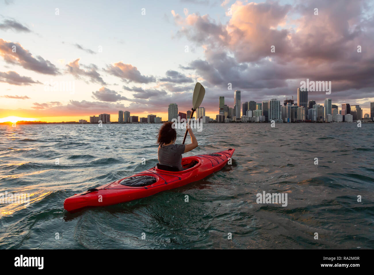 Adventurous girl kayaking in front of a modern Downtown Cityscape ...