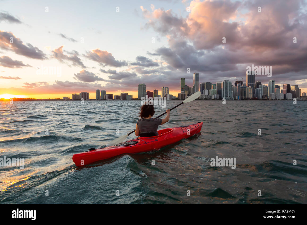 Adventurous girl kayaking in front of a modern Downtown Cityscape ...