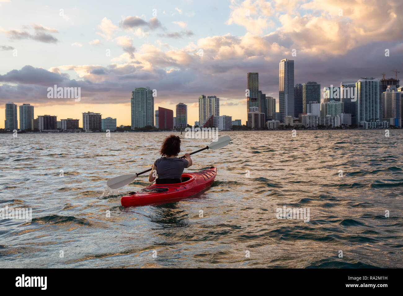 Adventurous girl kayaking in front of a modern Downtown Cityscape ...