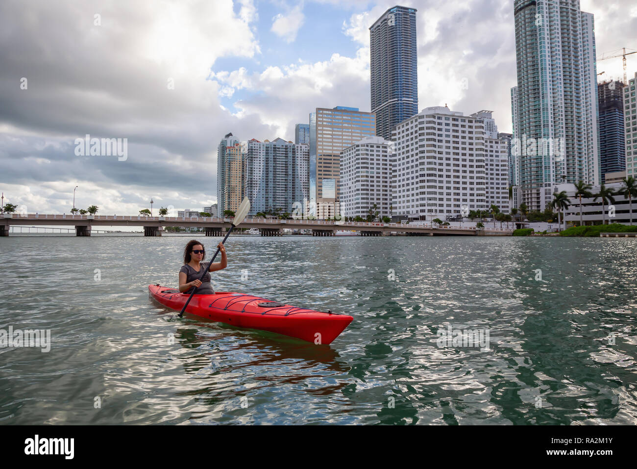 Adventurous girl kayaking in front of a modern Downtown Cityscape ...