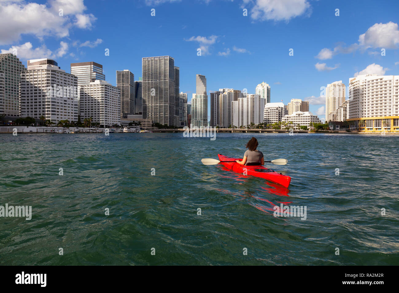 Adventurous girl kayaking in front of a modern Downtown Cityscape ...