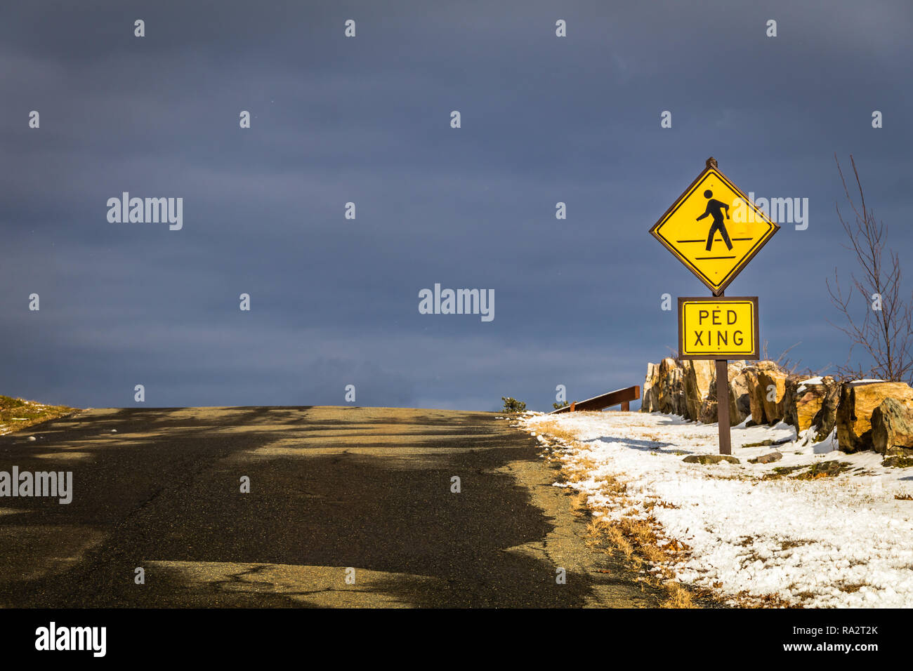 At the top of the hill, a pedestrian crossing sign and natural gray sky ...